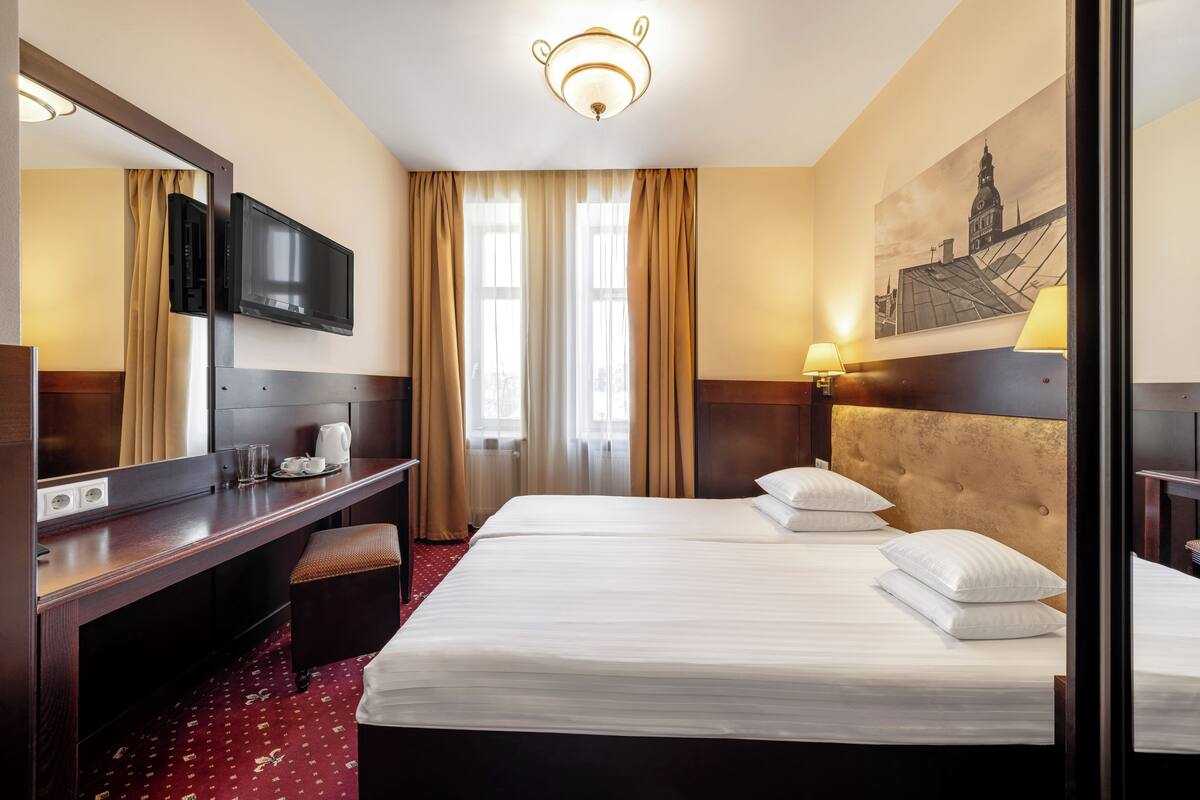 Quarto de hotel com duas camas, uma escrivaninha, televisão e um quadro na parede.