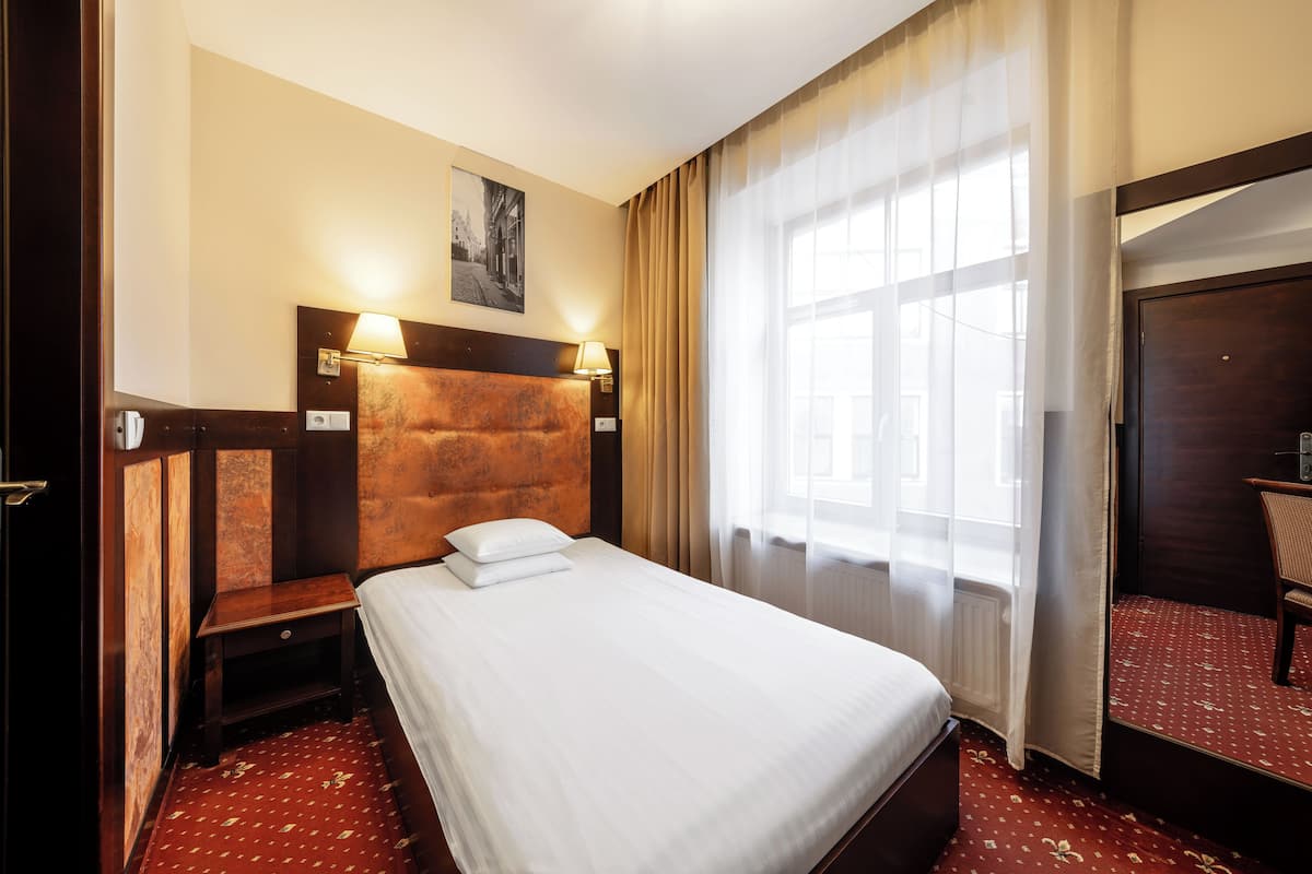 Quarto de hotel com cama, luminárias de cabeceira, mesa de cabeceira, janela com cortinas e espelho.