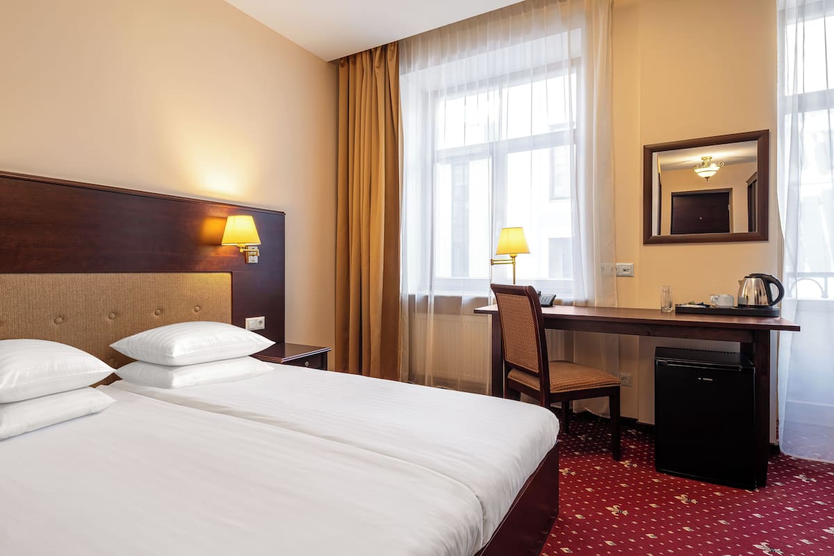 Quarto de hotel com uma cama, duas mesas de cabeceira, uma escrivaninha com cadeira, um espelho e um pequeno frigorífico.