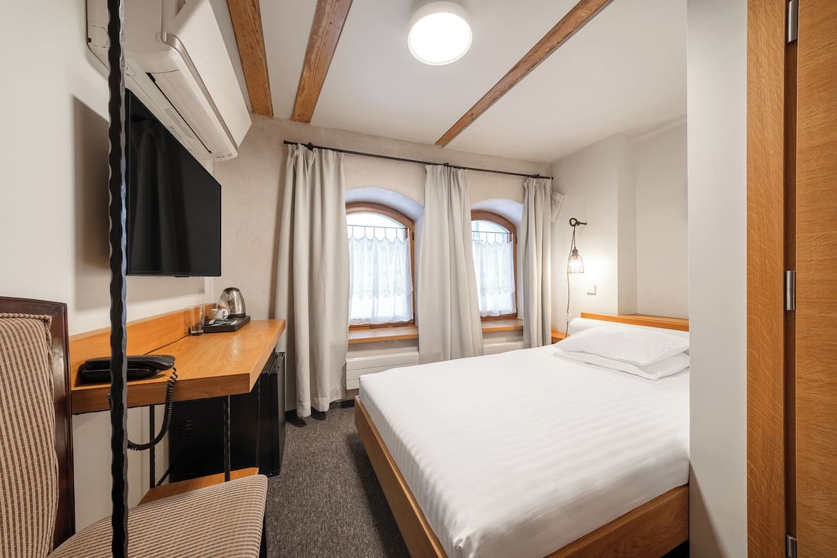 Quarto de hotel com uma cama, uma escrivaninha, uma televisão e uma janela com cortinas.
