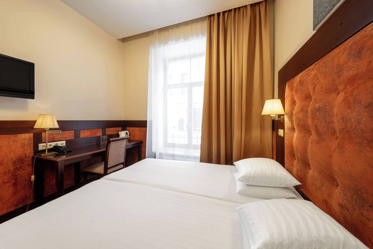 Quarto de hotel com cama, escrivaninha, cadeira e duas luminárias de cabeceira.