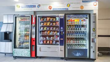 Três máquinas de venda automática de bebidas em um ambiente comercial, cada uma com diversas bebidas e lanches.