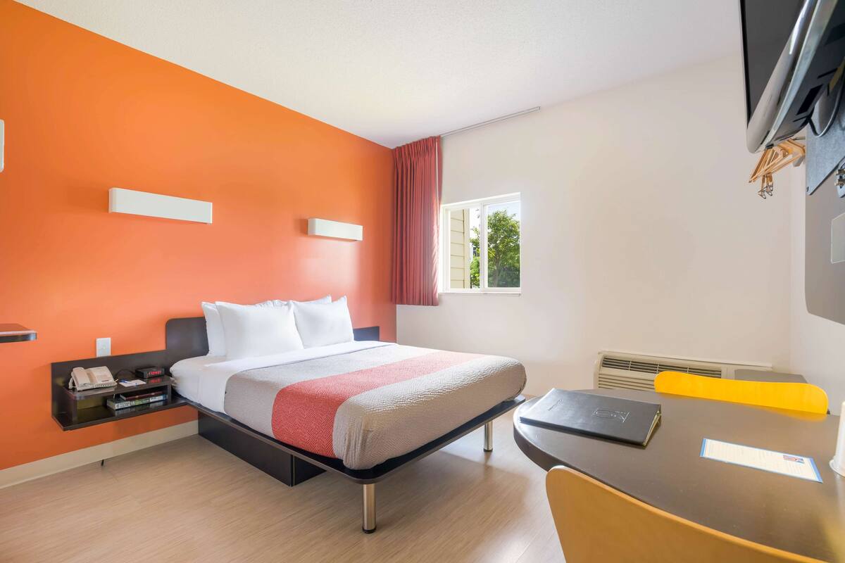 Quarto de hotel com uma cama, mesa de cabeceira e escrivaninha com cadeira.