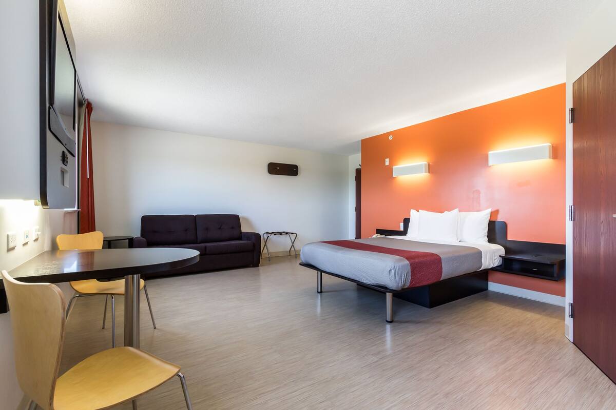 Quarto de hotel moderno com cama, sofá, mesa de jantar e cadeiras.