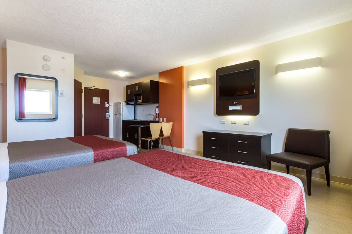 Quarto de hotel com duas camas, uma escrivaninha, uma cadeira, televisão e minibar.