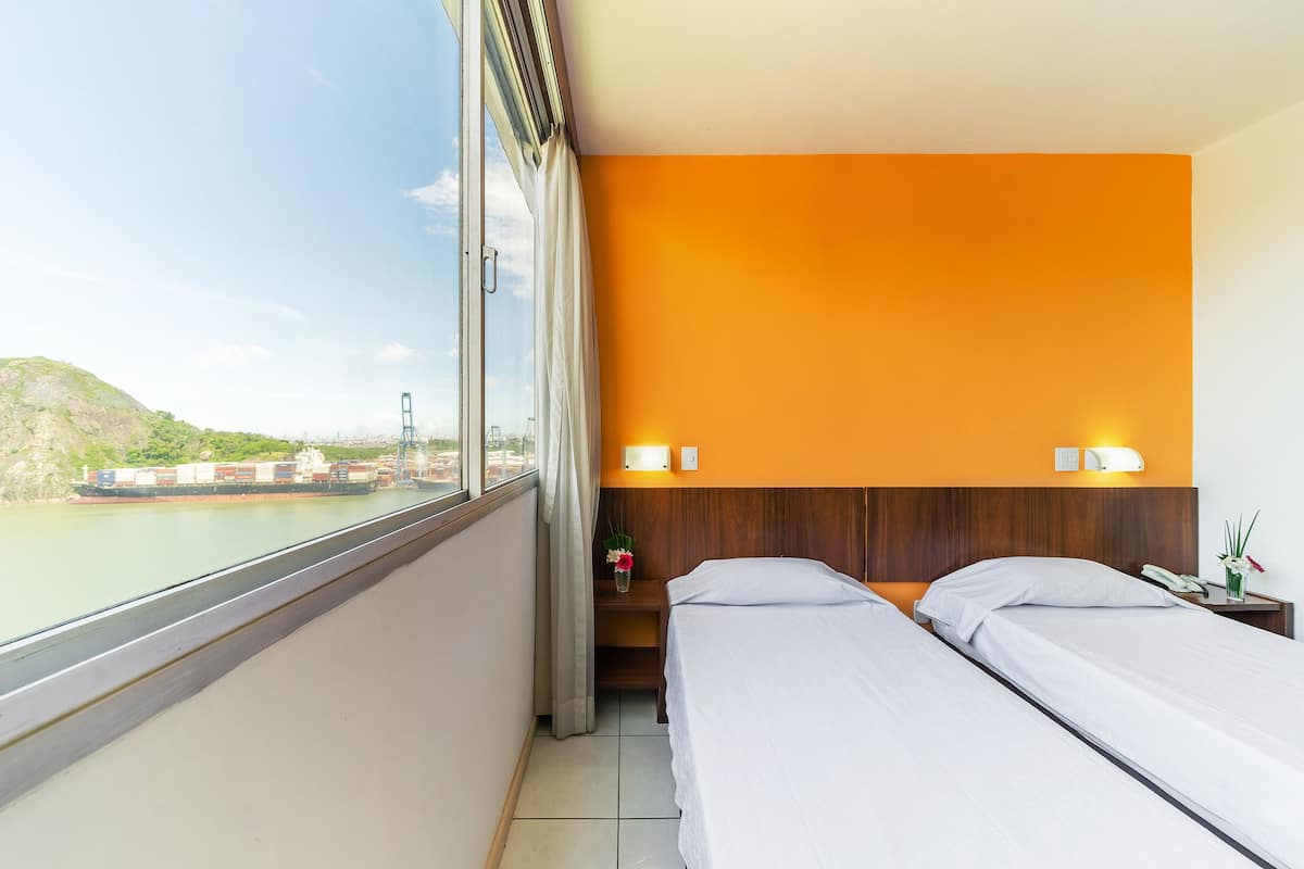 Quarto de hotel com duas camas, vista para um corpo de água e cabeceira de madeira.