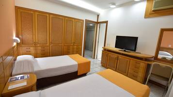 Quarto de hotel com duas camas, armários de madeira, uma televisão e uma escrivaninha.