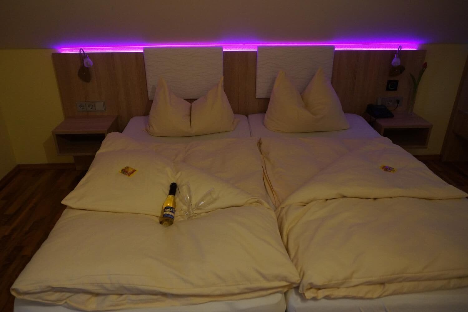 Cama bem arrumada com uma garrafa e um copo, cabeceira de madeira e mesa de cabeceira com abajur.