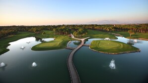 Um campo de golfe com lagoas, uma ponte e um clube.