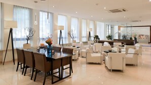 Um amplo saguão de hotel com área de refeições, assentos e balcão de recepção.