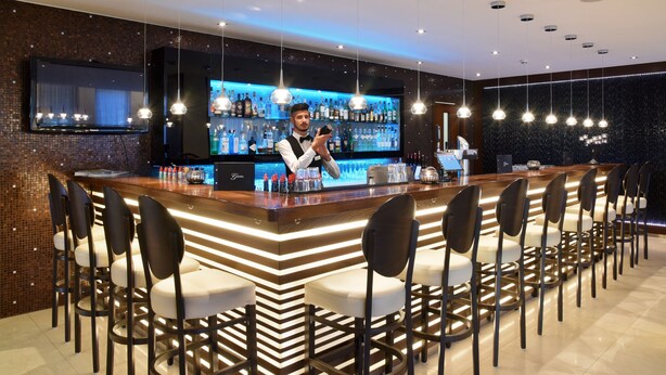 Uma área de bar moderna com um balcão comprido, vários banquetes, um bar bem abastecido e luminárias pendentes.