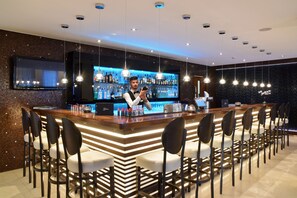 Uma área de bar moderna com um balcão comprido, vários banquetes, um bar bem abastecido e luminárias pendentes.