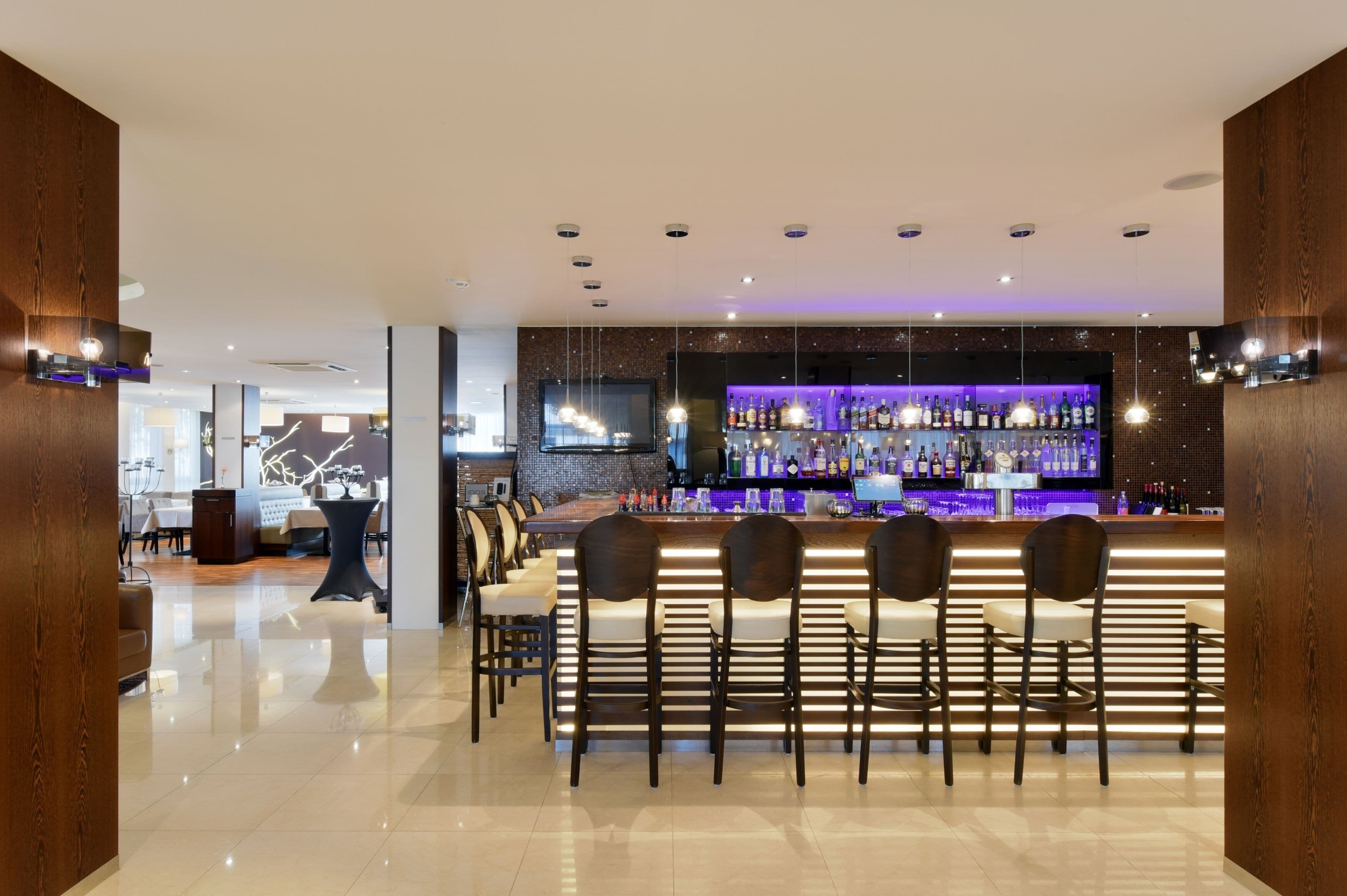 Uma área de bar moderna com piso polido, balcão de madeira e vários bancos.