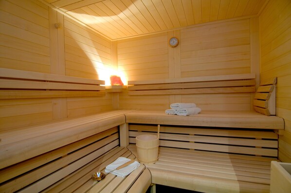 Uma sauna de madeira com bancos, um balde e toalhas.