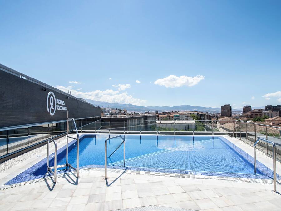 Piscina no terraço com vista para a cidade, um grande letreiro para Piedrosa Vaccines e um céu azul límpido.