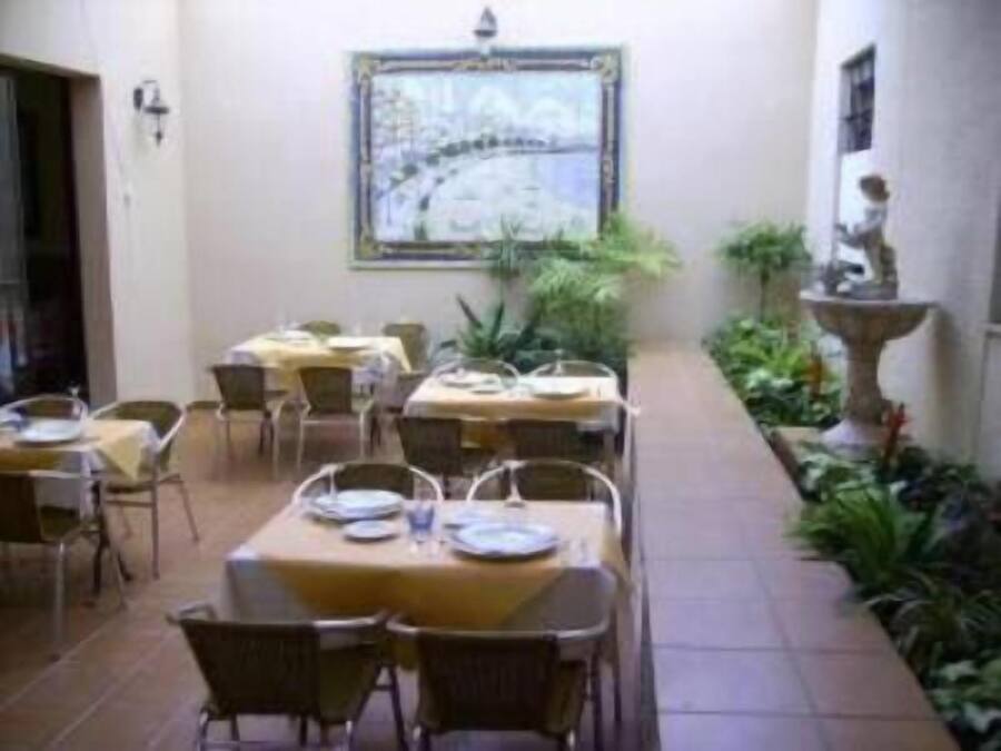 Uma área de refeições com mesas preparadas para dois, cadeiras e uma fonte decorativa.