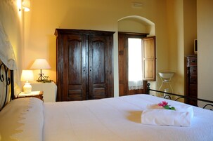 Quarto com cama grande, guarda-roupa de madeira e mesa de cabeceira com luminária.