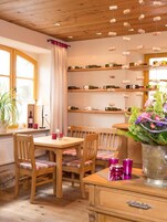 Uma área de refeições acolhedora com mobiliário de madeira, uma mesa com cadeiras, um vaso de flores e prateleiras com garrafas.