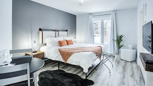Quarto moderno com cama, mesa de cabeceira, abajur e uma pequena mesa com uma cadeira.