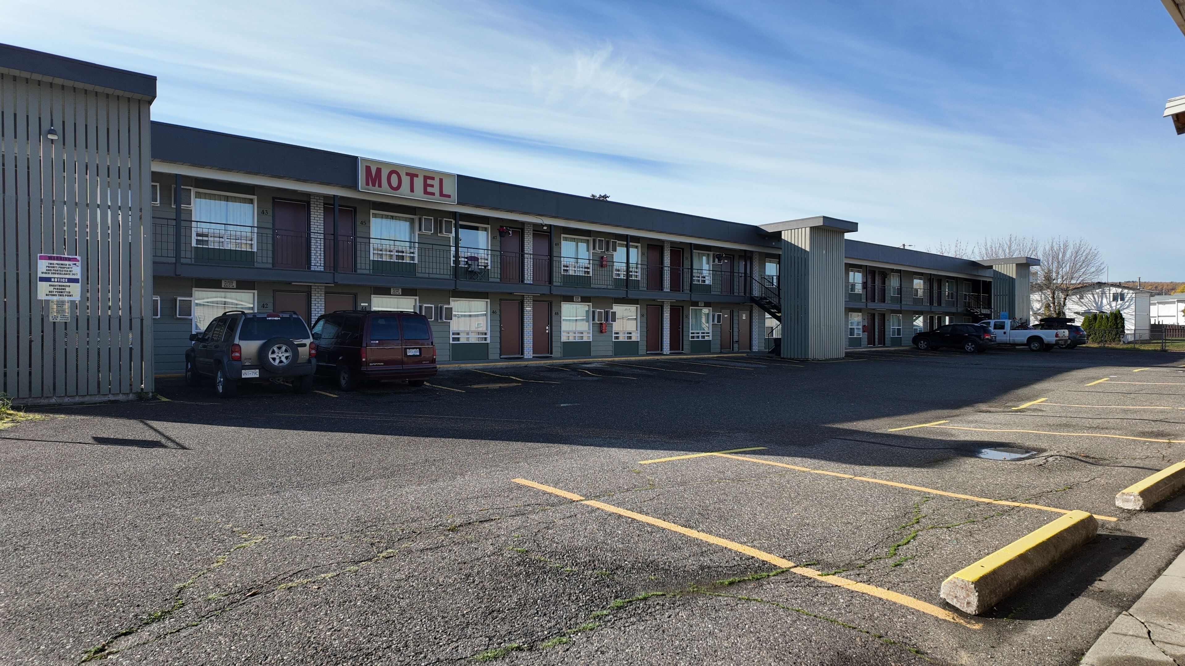 Um motel com várias vagas de estacionamento e uma fileira de quartos com entradas individuais.