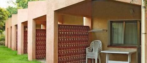 Um edifício térreo com varanda coberta, uma cadeira de plástico branca e uma mesa.