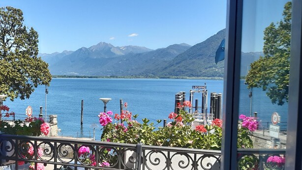 Uma varanda com mesa, flores e vista para um lago e montanhas.
