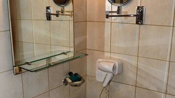 Casa de banho com lavatório branco, dois espelhos e uma estante de vidro.