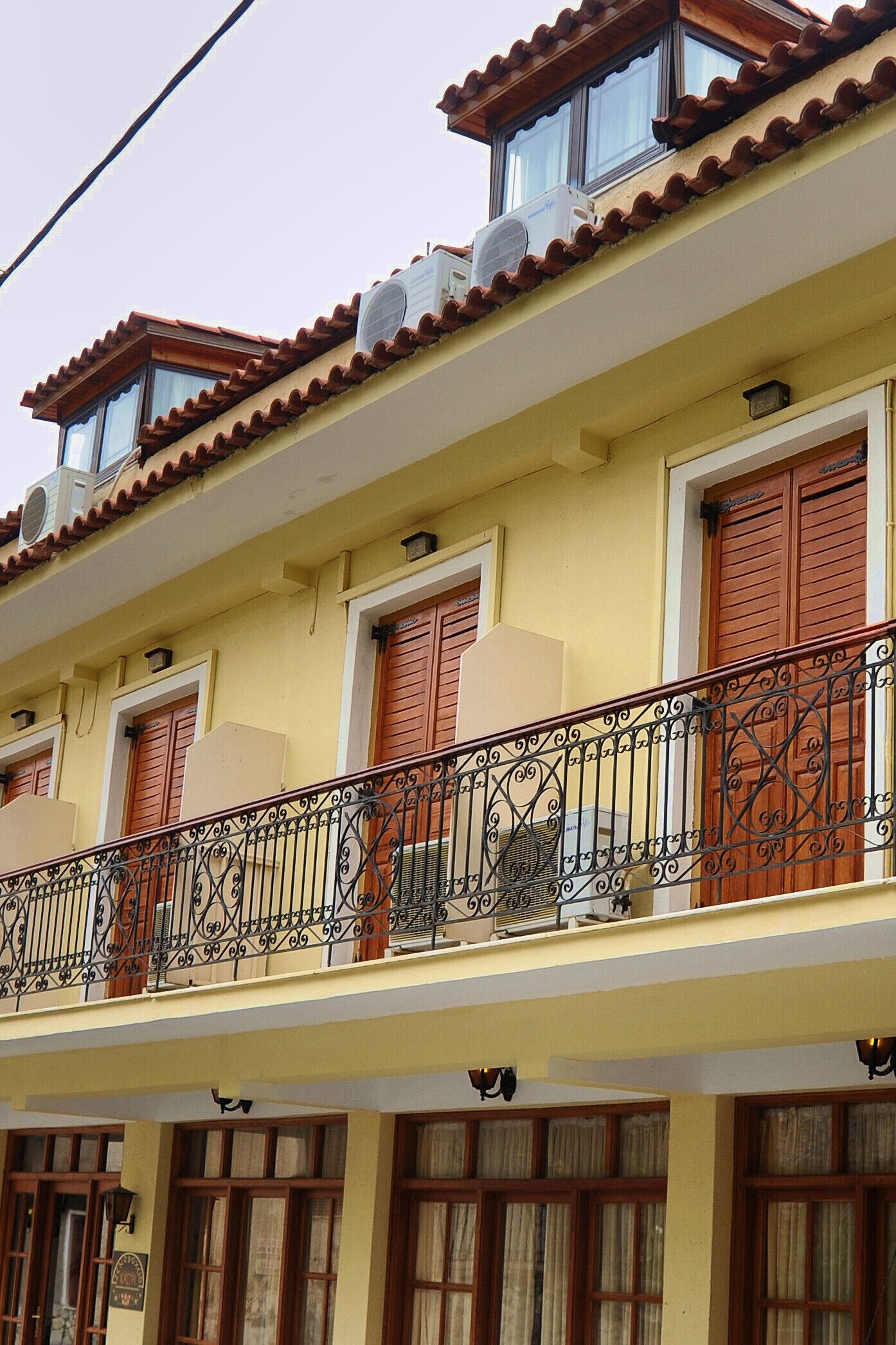 Um edifício com fachada amarela, telhado de telhas vermelhas e uma varanda com grades pretas detalhadas.