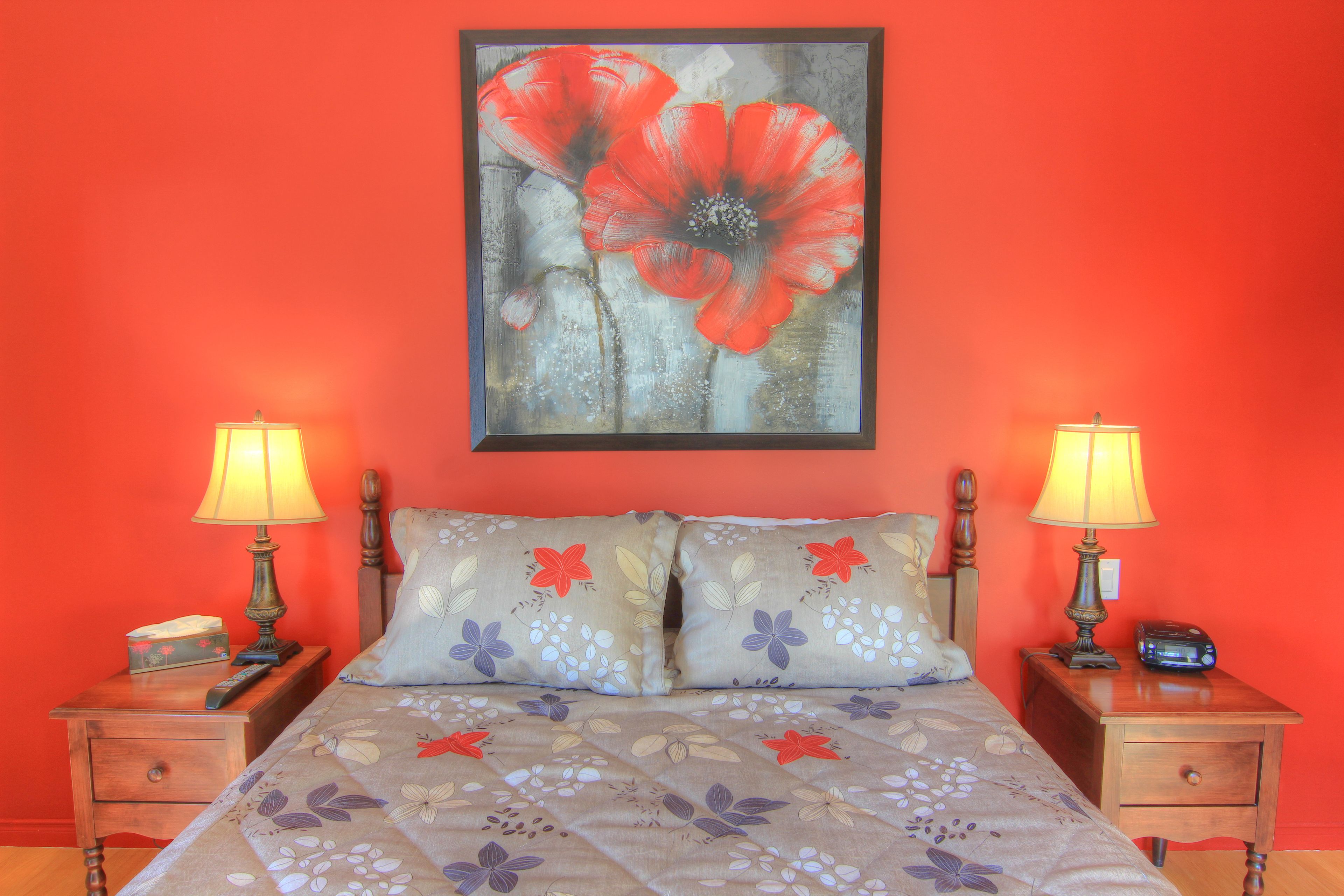 Quarto com cama, duas mesas de cabeceira, duas luminárias e uma pintura floral emoldurada na parede.