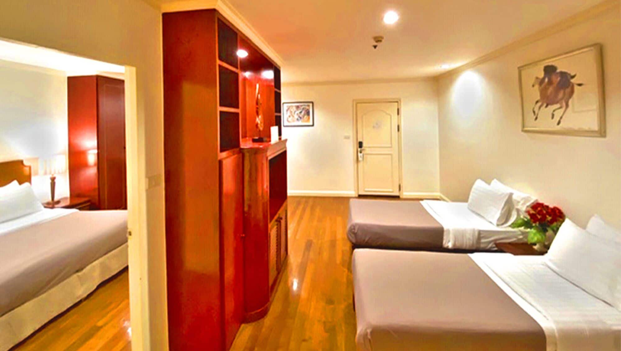 Quarto de hotel com duas camas de solteiro, piso de madeira, parede em vermelho e uma porta, além de um quadro pendurado na parede.