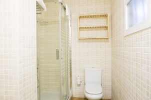 Um banheiro pequeno e revestido com azulejos, com box de vidro, vaso sanitário e porta-toalhas.