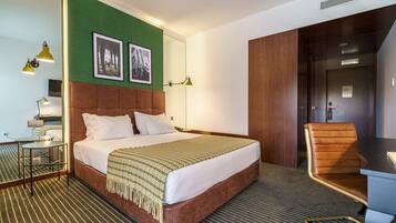 Quarto de hotel com uma cama grande, uma escrivaninha, uma cadeira e duas fotos emolduradas na parede.