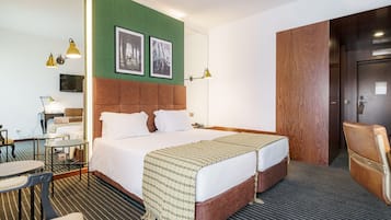 Quarto de hotel com uma cama grande, uma escrivaninha, duas cadeiras, uma parede verde e uma porta de madeira.