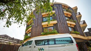 Uma carrinha branca estacionada em frente a um edifício moderno com um design arquitetónico único, apresentando jardins verticais e varandas.