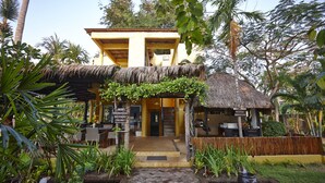 Um resort tropical com estrutura de telhado de palha, área de estar externa e vegetação exuberante.