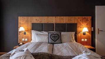 Quarto com cabeceira de madeira, duas luminárias de apoio, um travesseiro em formato de coração e um tapete fofinho.