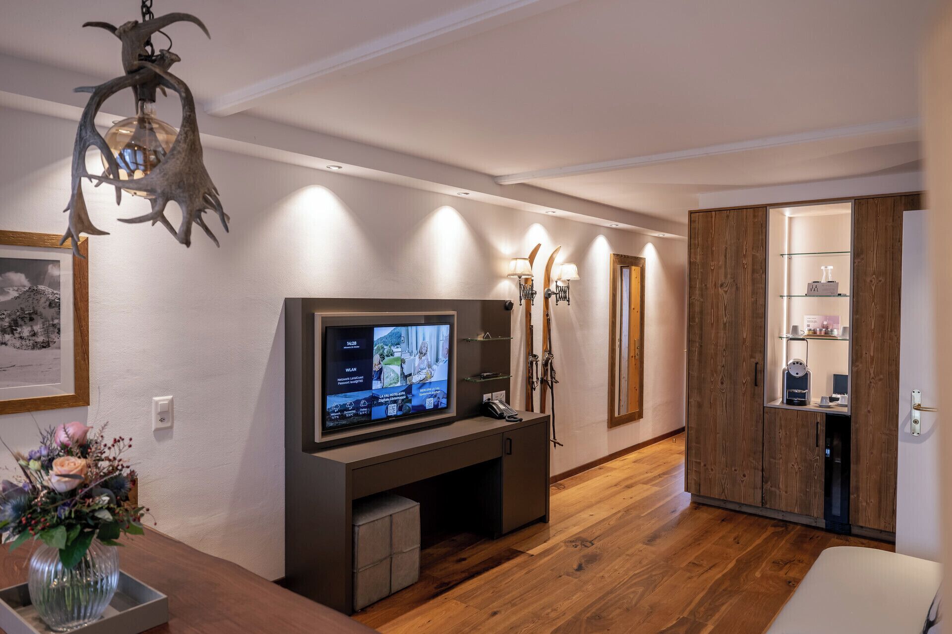 Uma sala de estar moderna com televisão de tela plana, piso de madeira e um lustre decorativo com chifres.