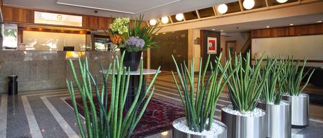 Um hall de entrada com balcão de recepção, plantas em vasos e um carpete estampado.