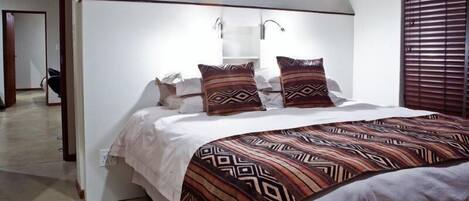 Quarto moderno com uma cama grande, duas almofadas decorativas e uma mesinha de cabeceira.