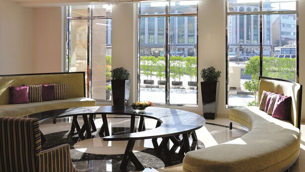 Uma área de estar moderna com um sofá curvo, uma mesa redonda e grandes janelas com vista para a cidade.