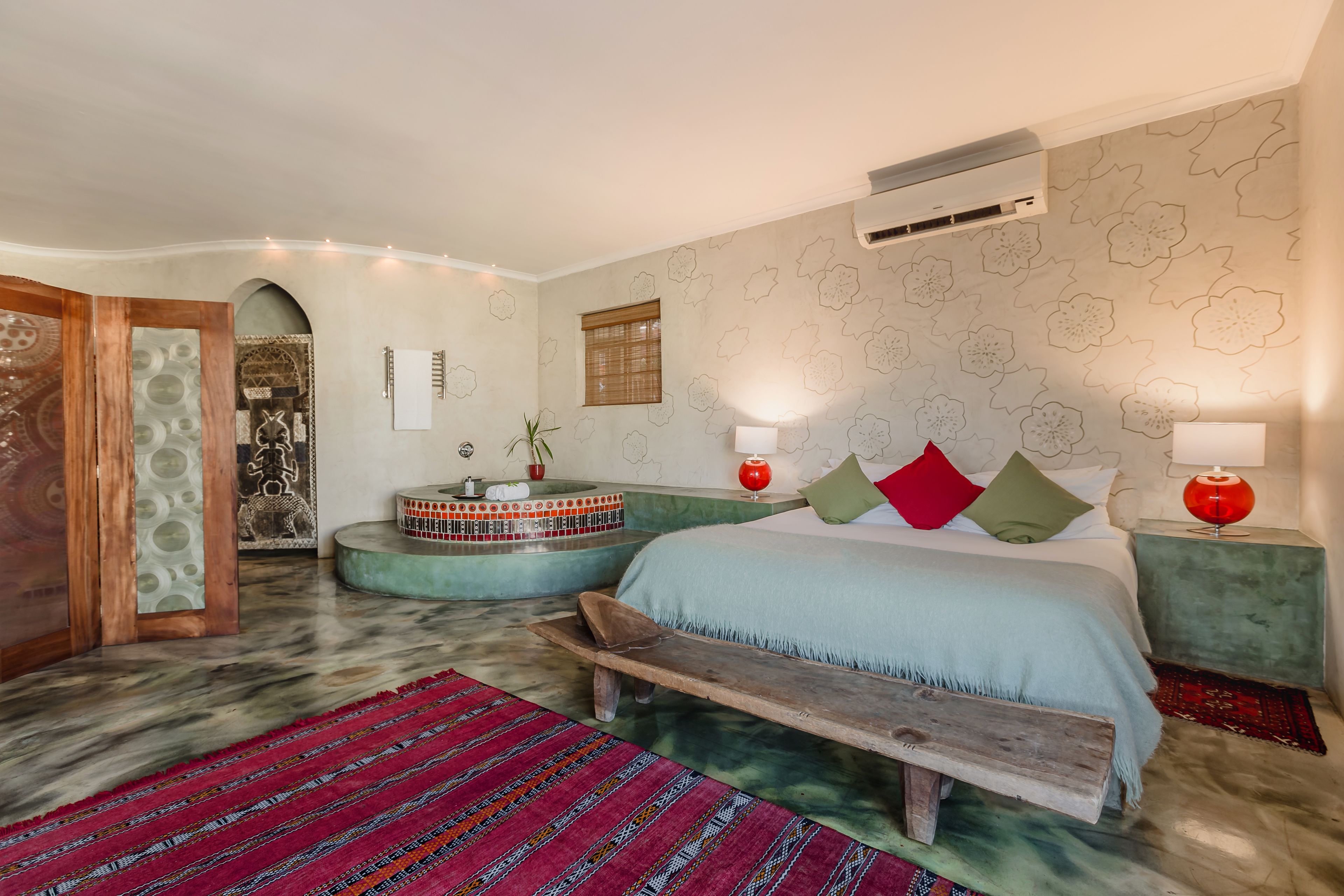Quarto com cama grande, um banco, área de estar circular e ar condicionado fixado na parede.