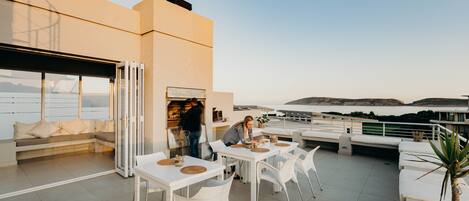 Terraço no telhado com mobiliário branco, espaço para churrasco e vista para a paisagem.