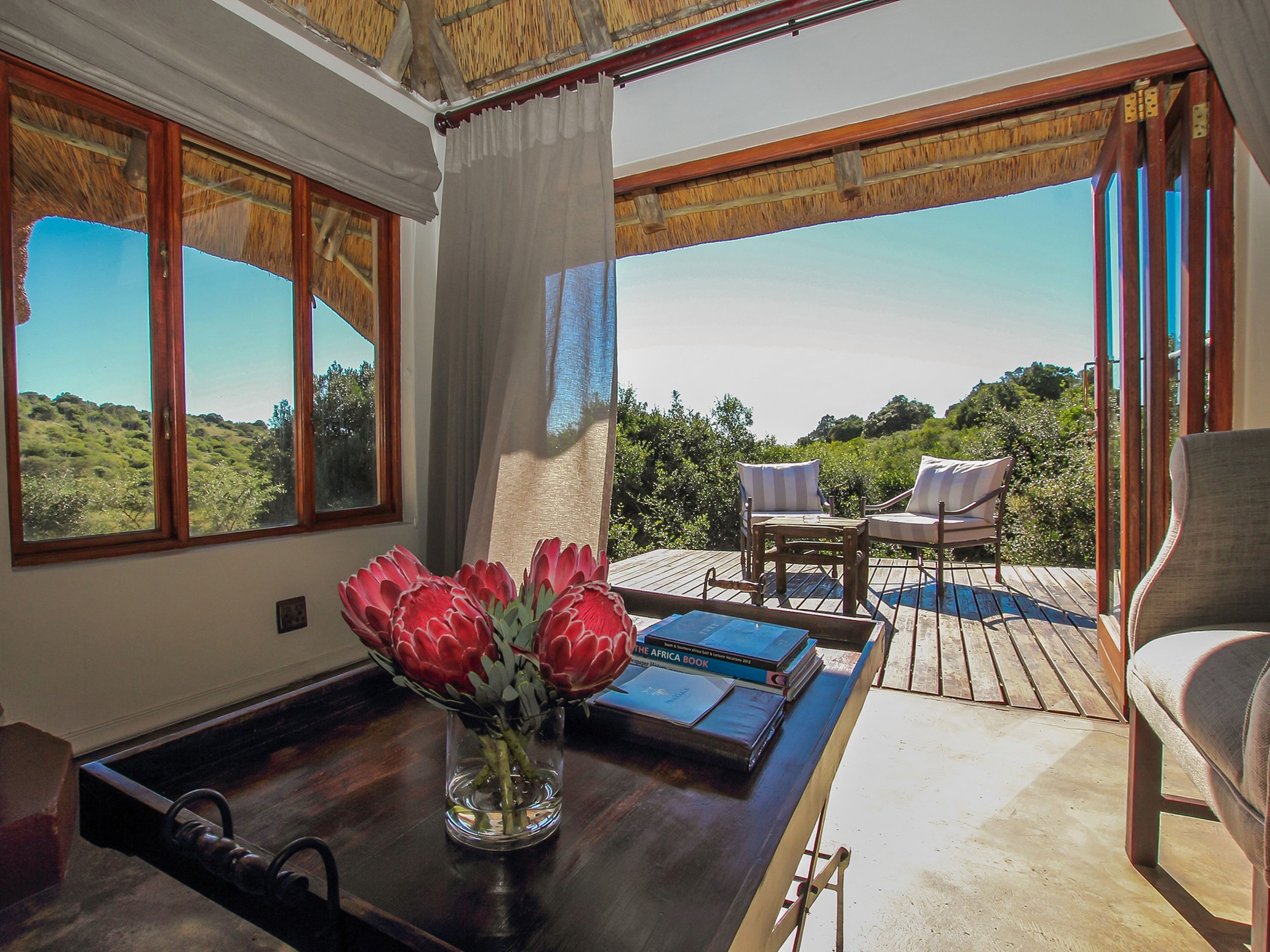Um quarto com uma mesa de madeira, um vaso com flores vermelhas e duas cadeiras.