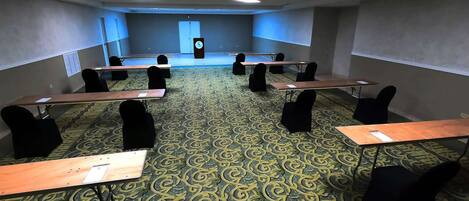Uma sala de conferências com carpete estampado, cadeiras pretas e mesas de madeira.