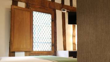 Quarto com cama, janela de madeira e parede com vigas aparentes.