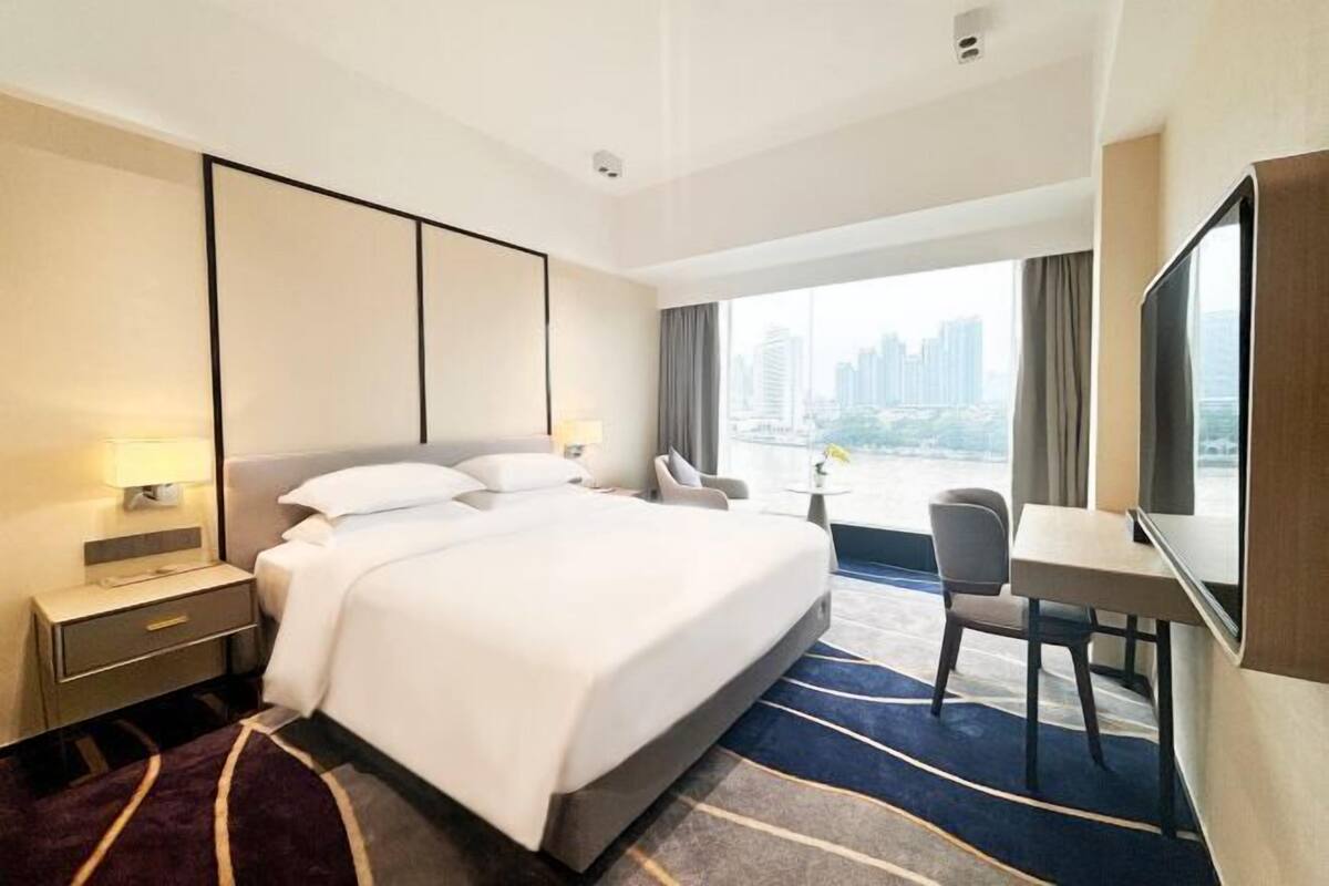 Quarto de hotel com cama grande, escrivaninha, cadeira, televisão e vista da cidade.