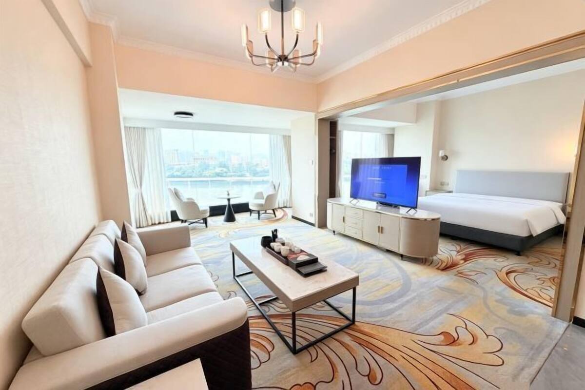 Quarto de hotel com sofá, mesa de centro, televisão, cama e vista para a cidade.
