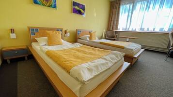 Quarto de hotel com duas camas, uma escrivaninha, uma cadeira e uma janela com cortinas.