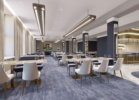 Uma zona de refeições moderna com tetos altos, iluminação pendente e um bar central.