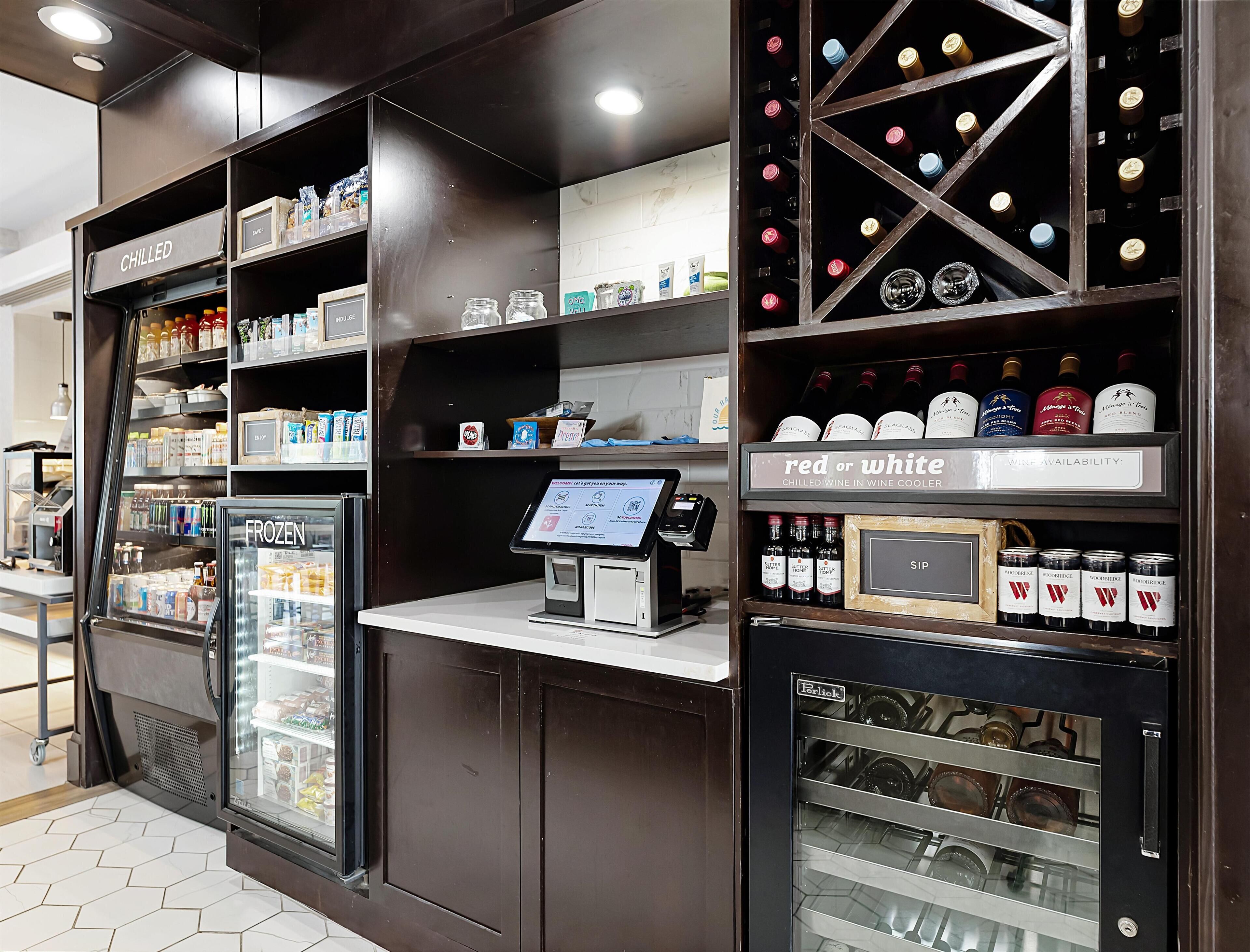 Clarabox refrigerada para vinho com tela digital de seleção, área refrigerada com produtos embalados e exposição de garrafas de vinho.